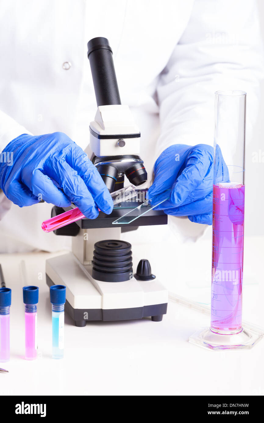 Lab technician working with equipment: tweezers, microscope, test tubes ...