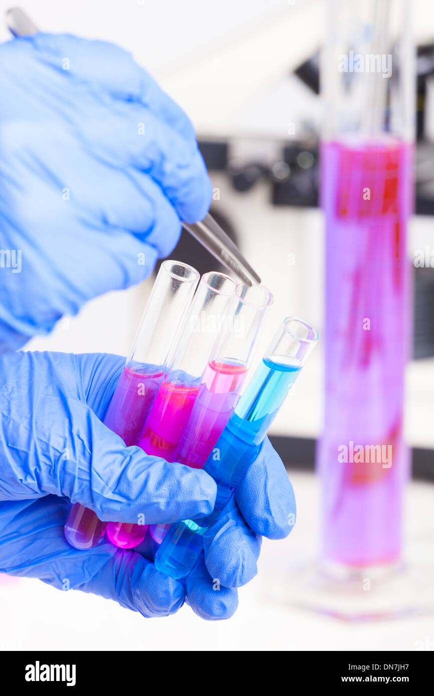 Lab technician working with equipment: tweezers, microscope, test tubes ...