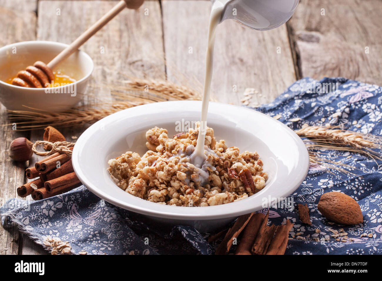 Plate of muesli with pouring milk, cinnamon and nuts over old wooden ...