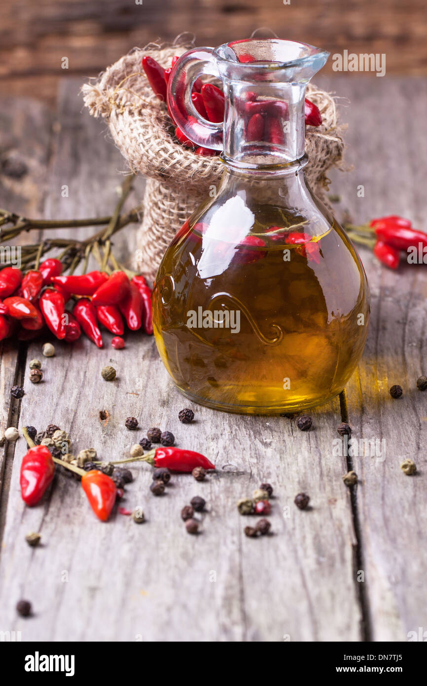 Glass bottle of olive oil with red hot chili peppers over old wooden ...