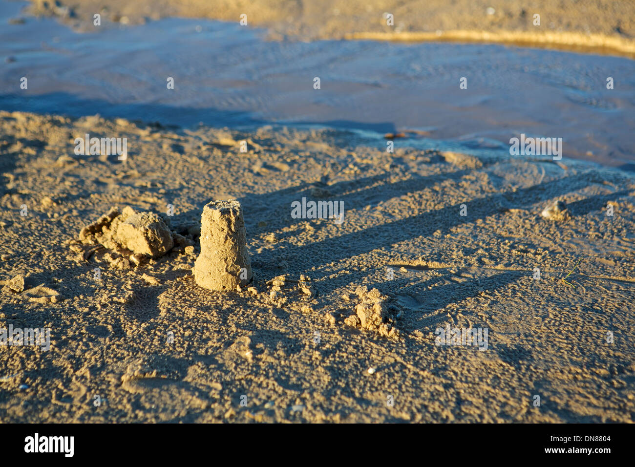 Remnants of a sand castle cast a shadow on a beach with a small river ...