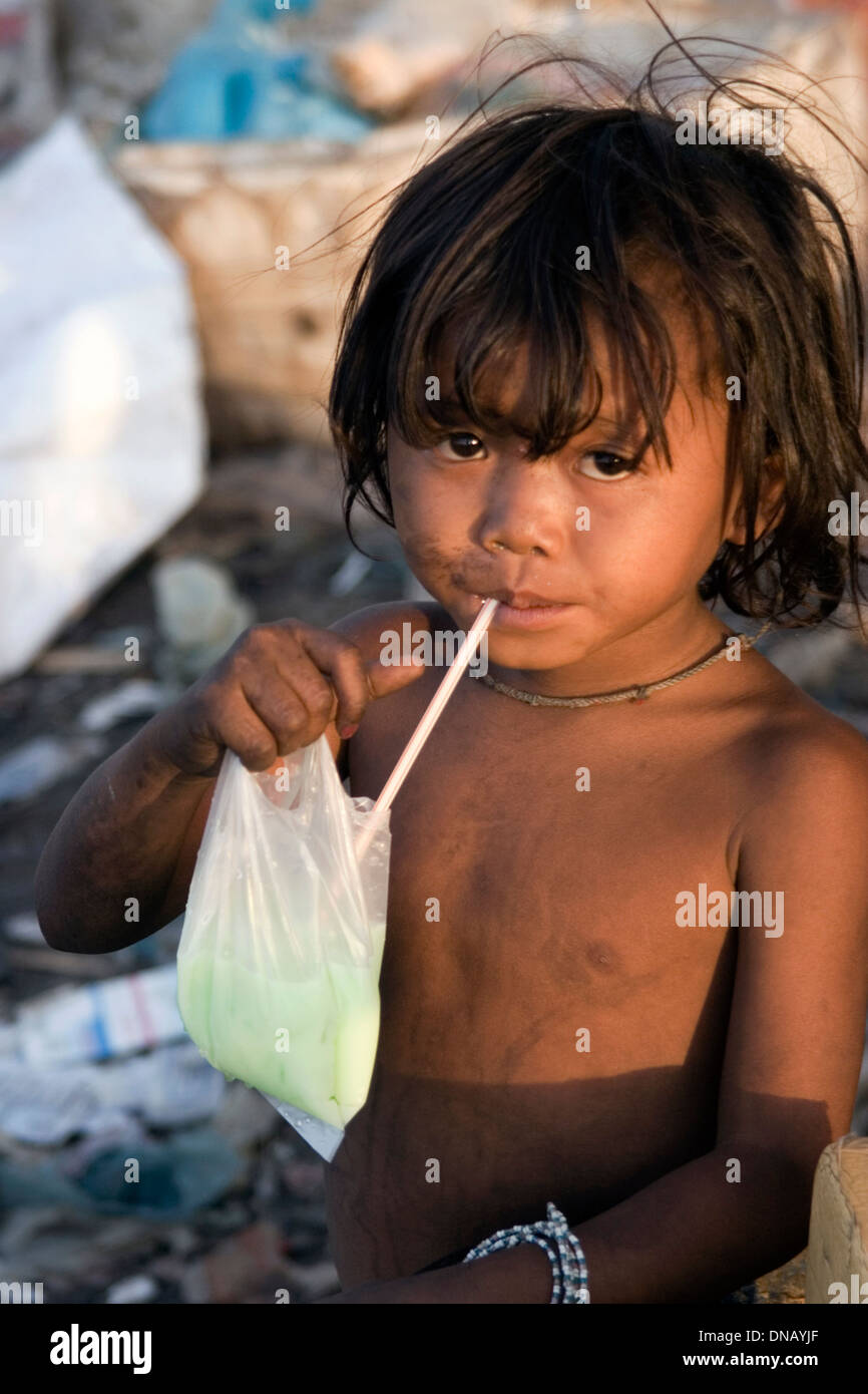 A young child laborer girl is drinking a refreshment in a garbage dump ...