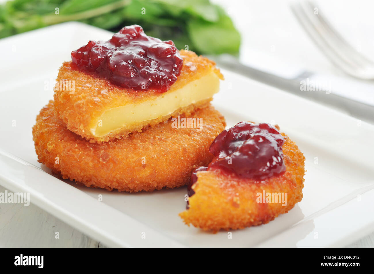 Breaded and baked camembert with cranberry sauce on white plate closeup ...