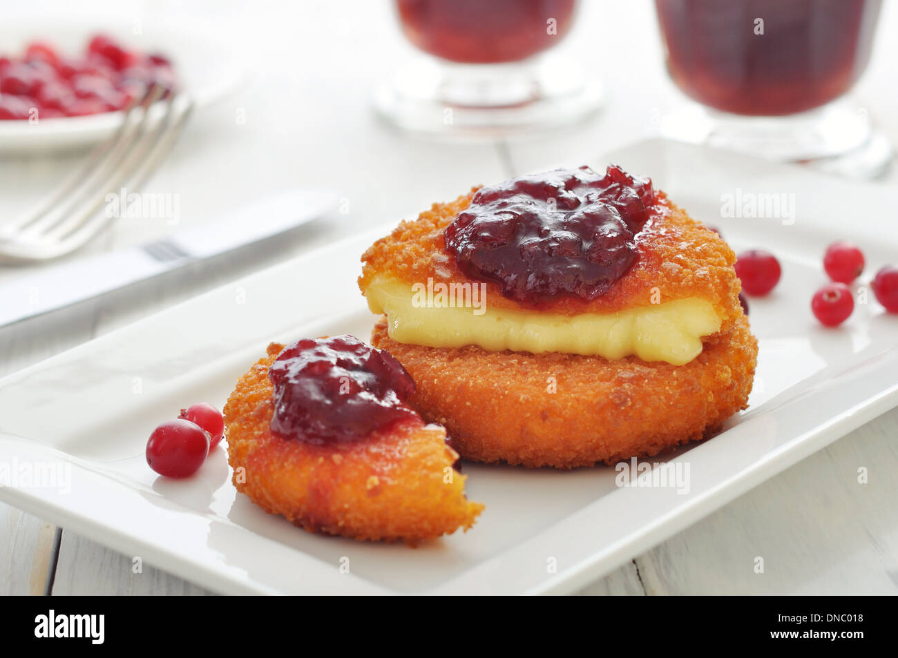 Breaded and baked camembert with cranberry sauce on white plate closeup ...