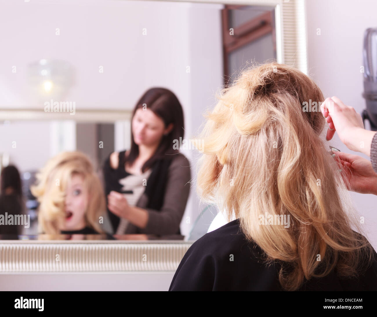Surprised shocked girl with blond wavy hair by hairdresser. Hairstylist ...