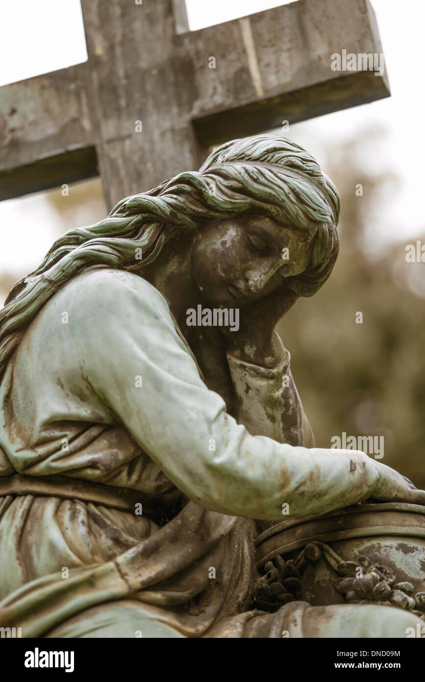 Old gravestone statue of sad thinking woman next to a cross Stock Photo ...