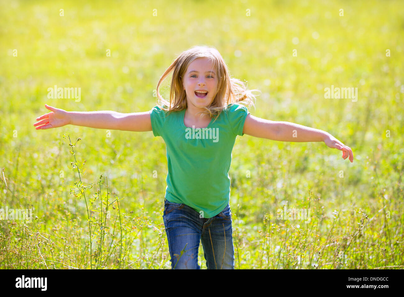 Blond kid girl happy running open hands smiling in outdoor green meadow ...