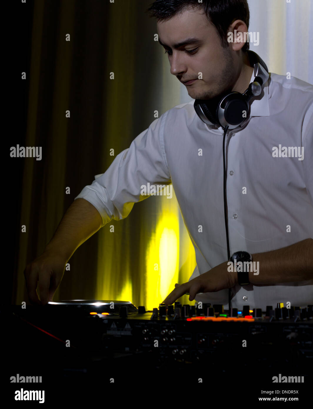 DJ standing at his deck mixing music in the darkness at a disco or ...
