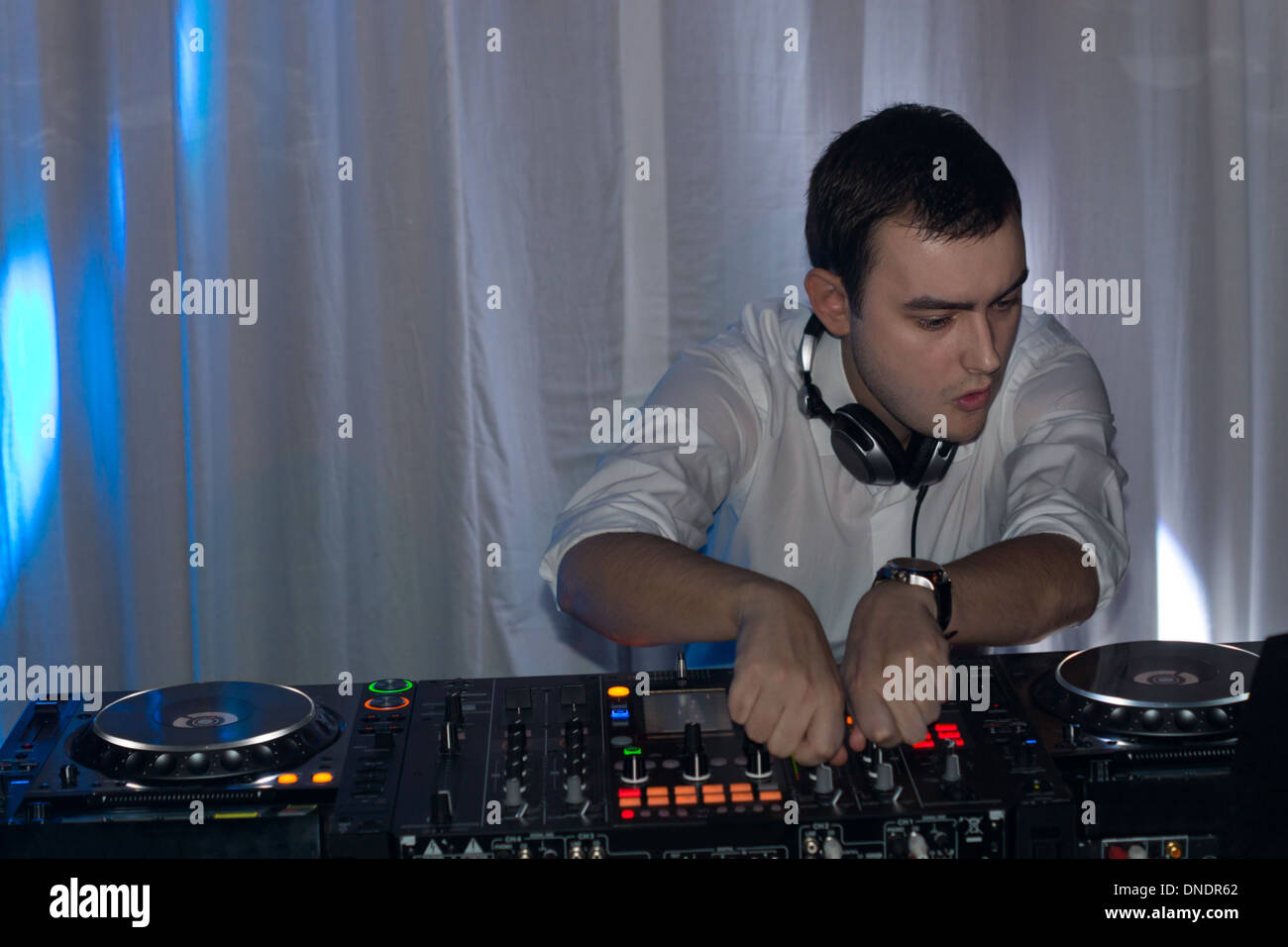 Handsome young disc jockey mixing music at a deck in a nightclub as he ...