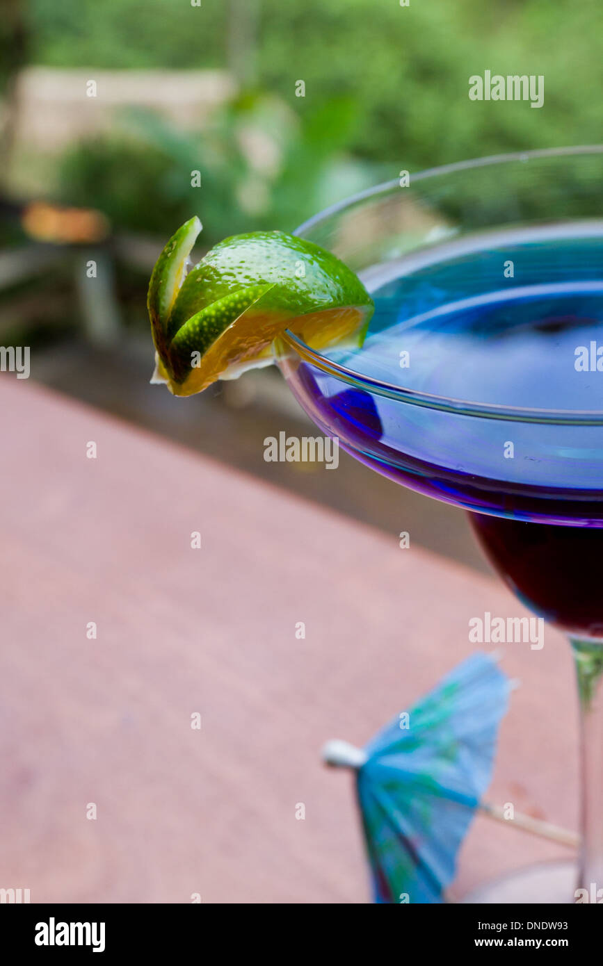 blue rain forest drink served on a wooden ledge with the jungle in the ...