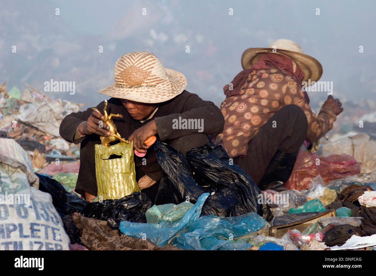 A scavenger woman is searching through garbage for items of value at ...