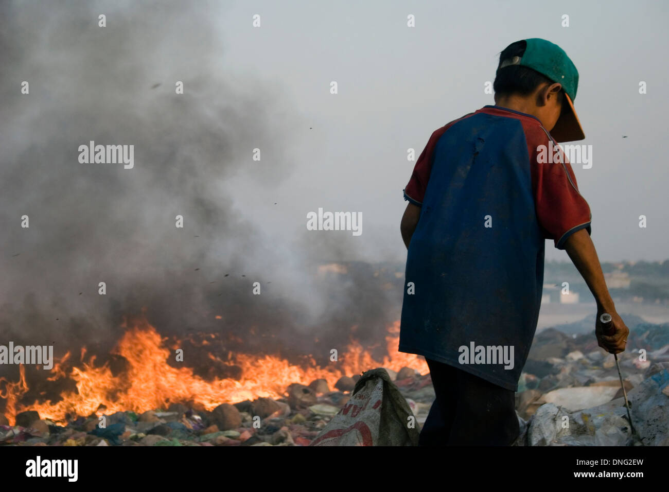 A young child laborer boy is working near flaming piles of garbage at ...
