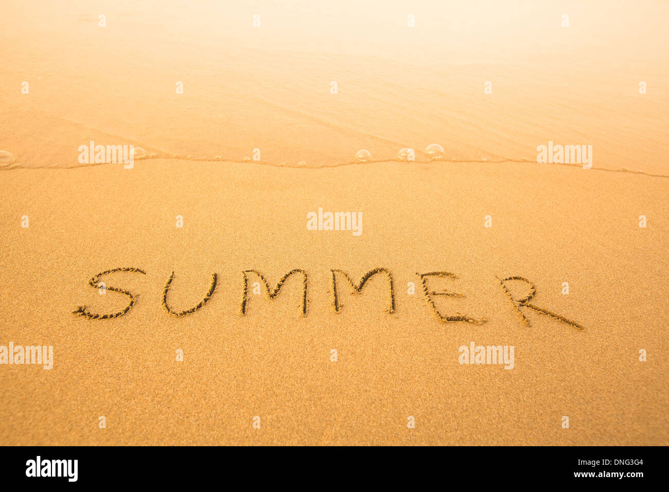 Summer - text written by hand in sand on a beach, with a soft wave ...