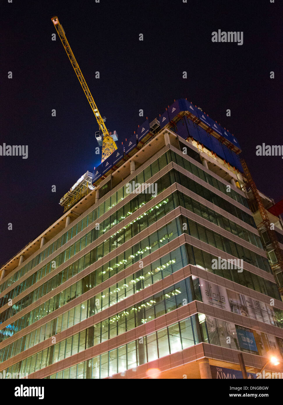 Tower construction crane rises above a lit building under construction ...