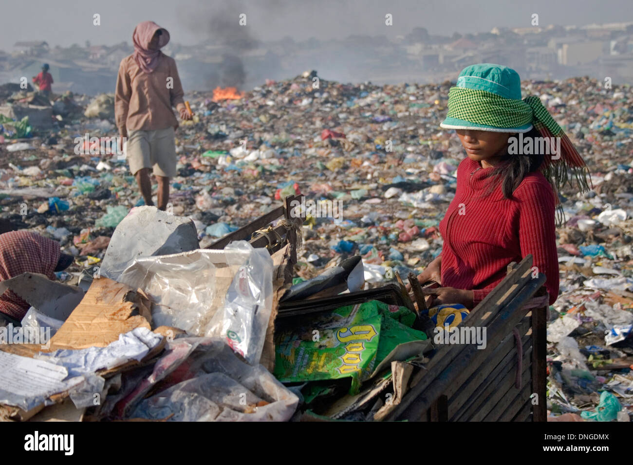 A child laborer girl is loading a wooden cart with garbage at the toxic ...