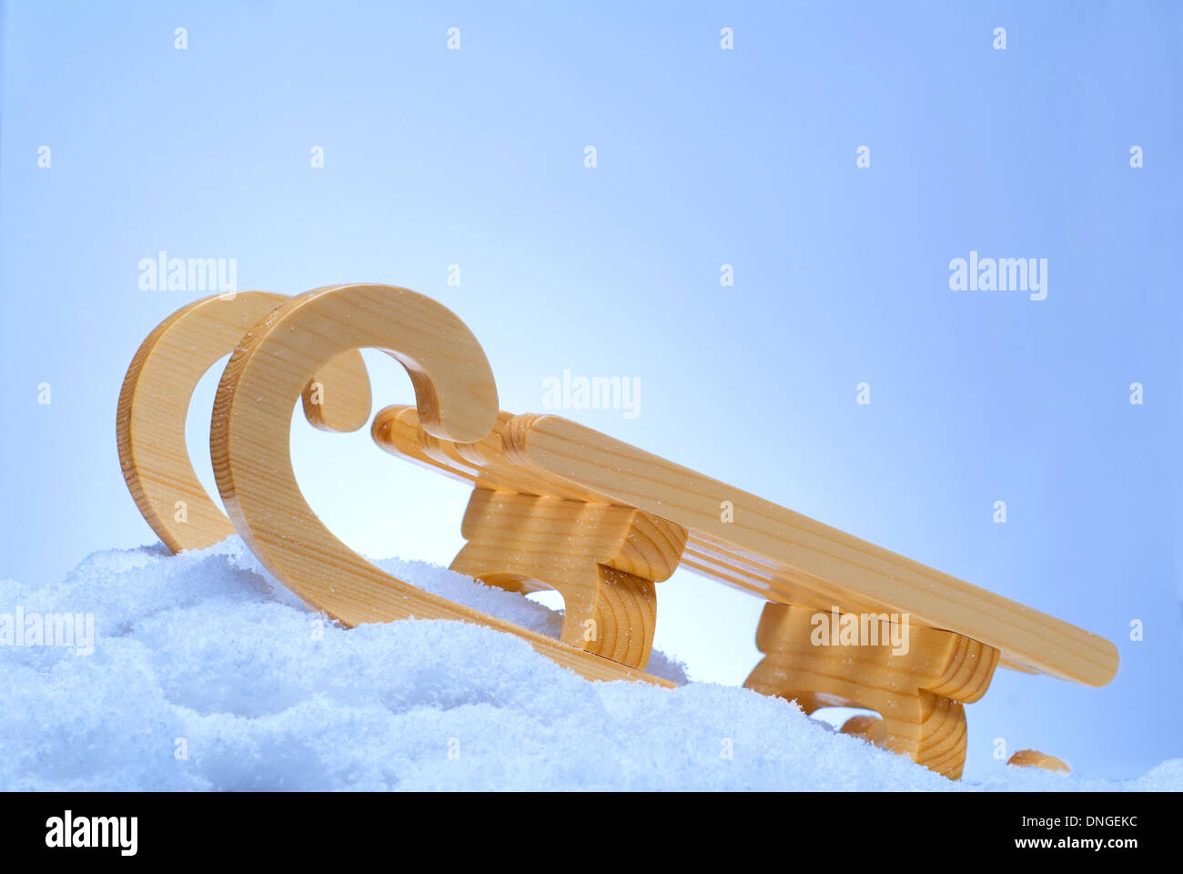 Small wooden toy sled on snow at clean light blue background. Low point ...