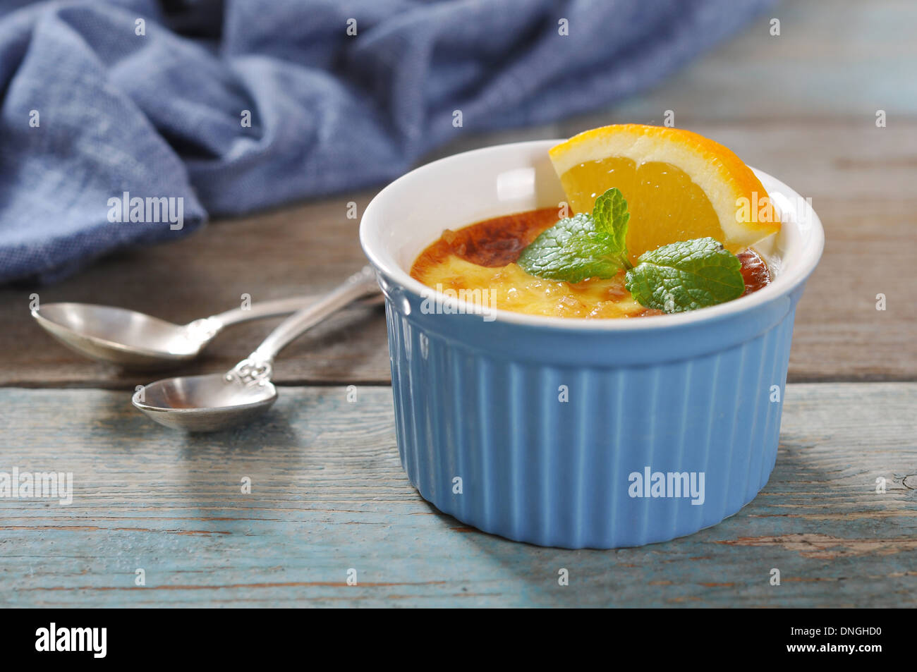 The creme brulee in ceramic baking mold with orange on wooden table ...