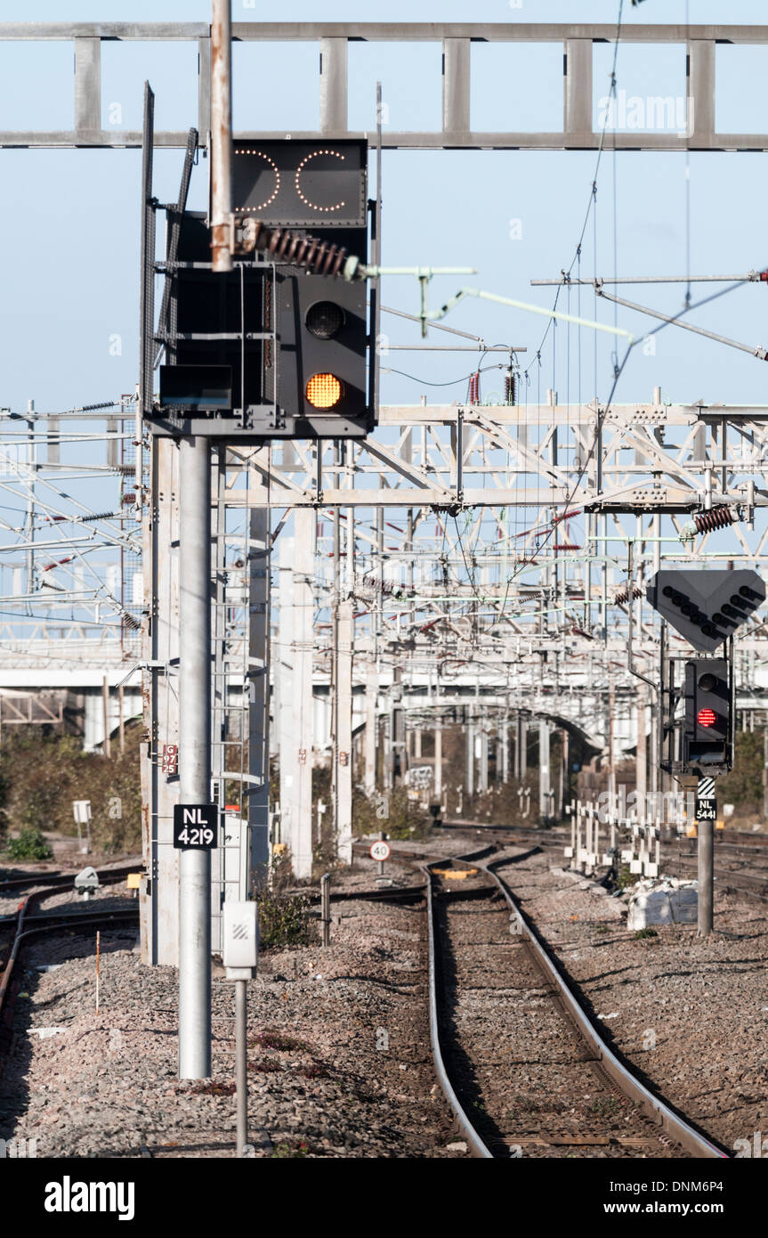 A yellow and red railway signal amongst the complex overhead power ...