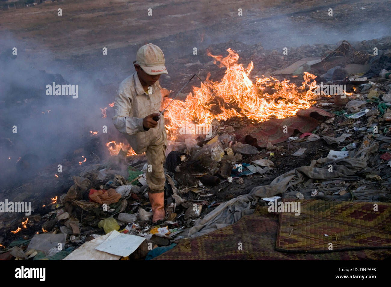 A young child laborer boy is working near a pile of burning garbage at ...
