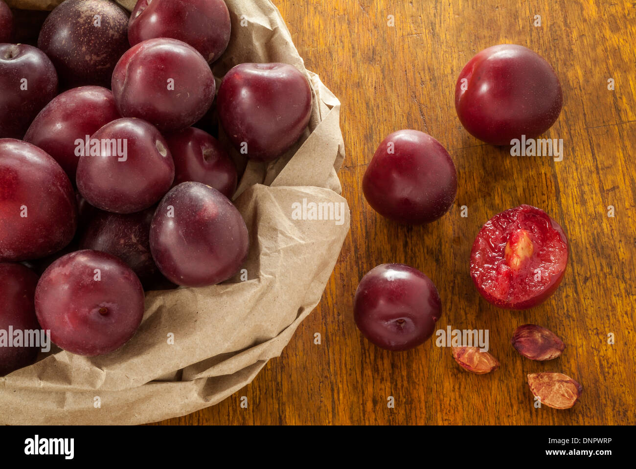 An image of red plums in a crumpled brown paper bag on a wood table ...