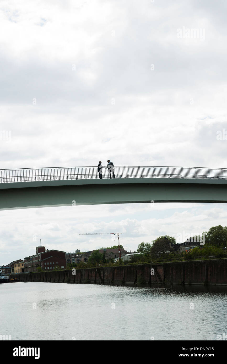 Silhouette of mature businessmen standing on bridge shaking hands ...