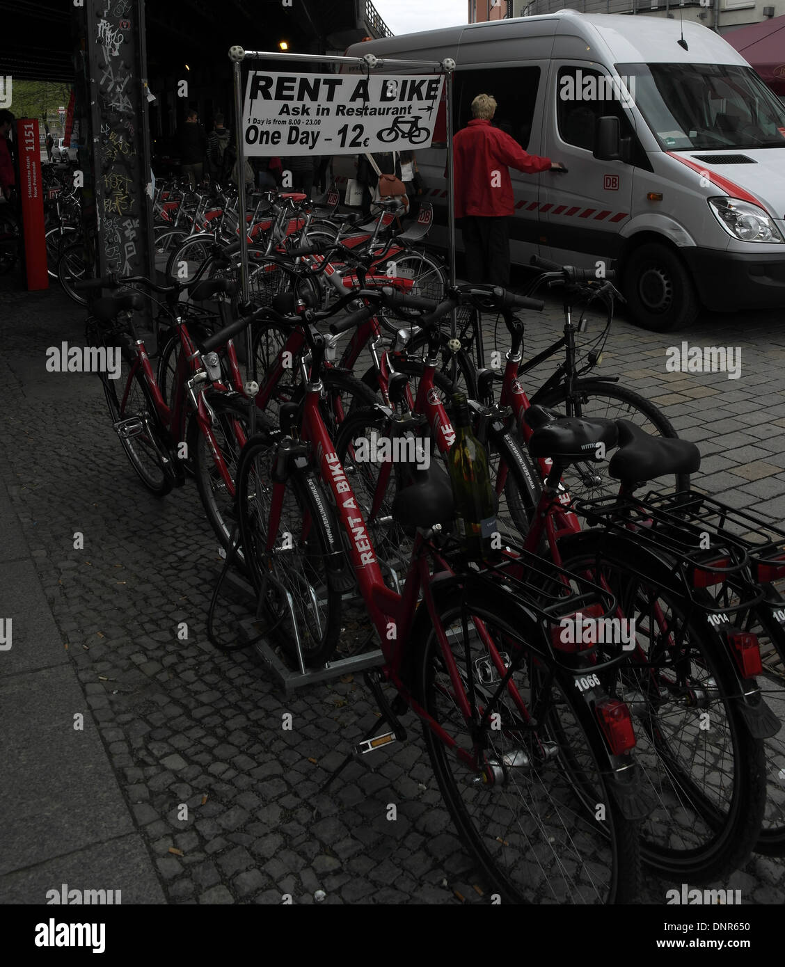 White minibus by many 'rent-a-bike bicycles at the railway bridge ...