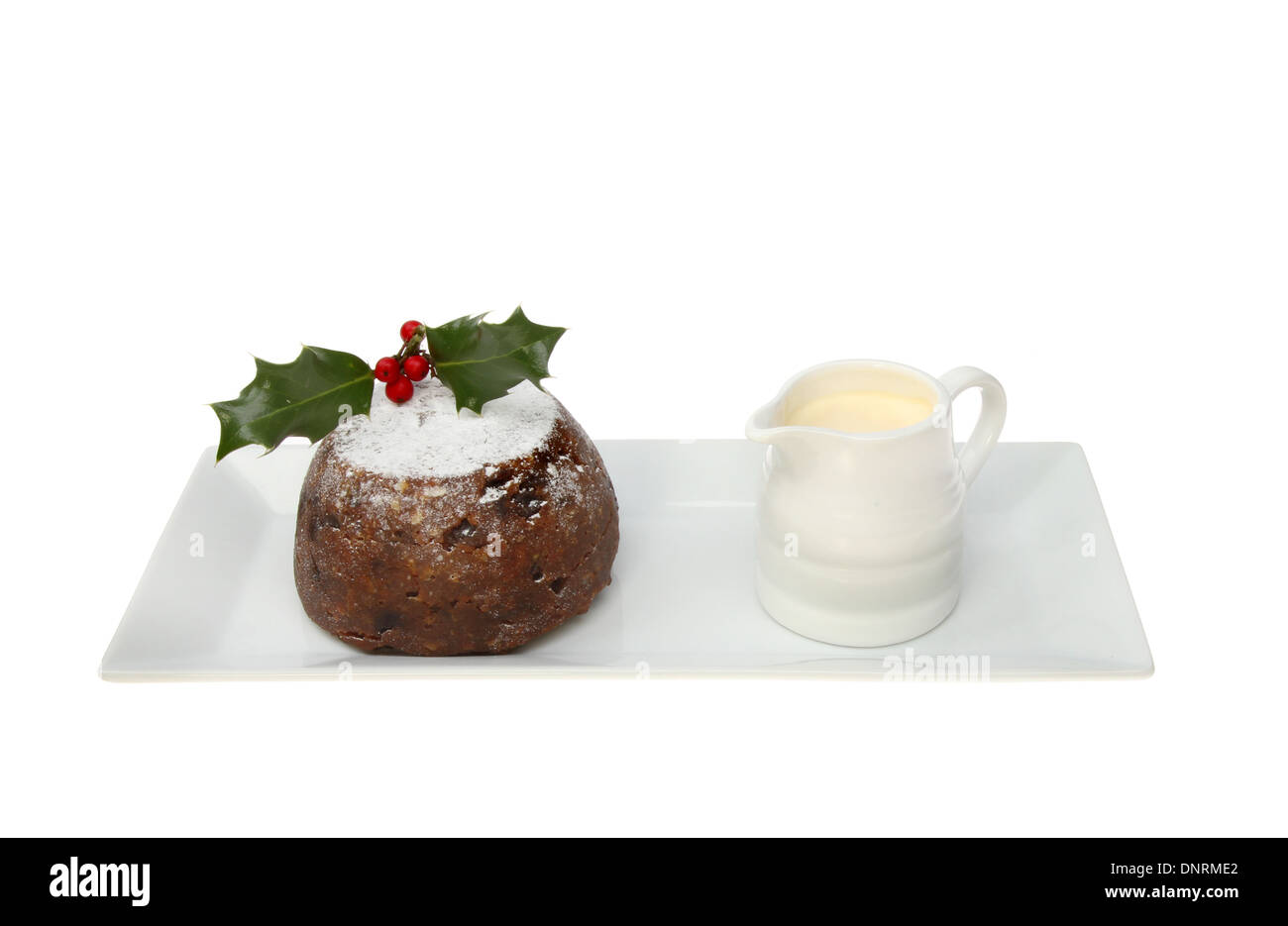 Holly decorated Christmas pudding with a jug of cream on a rectangular ...
