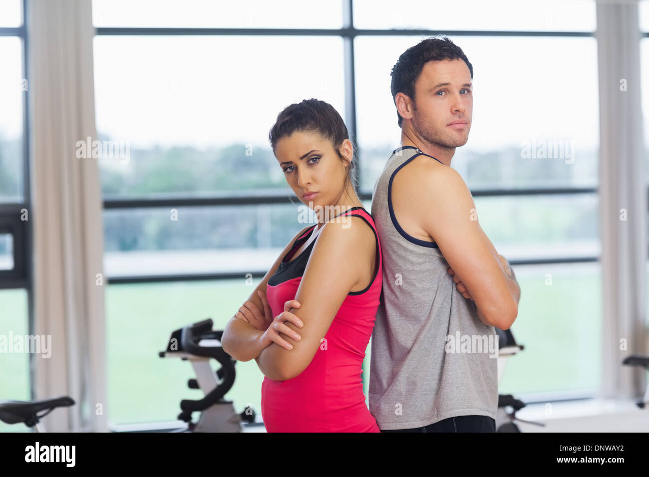 Serious young woman and man standing back to back in gym Stock Photo ...