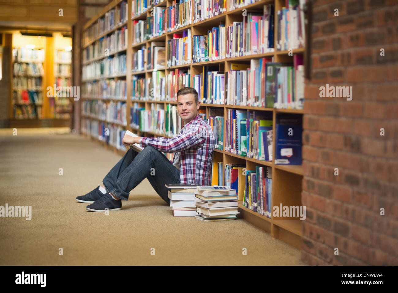 Smiling student sitting on library floor reading Stock Photo - Alamy