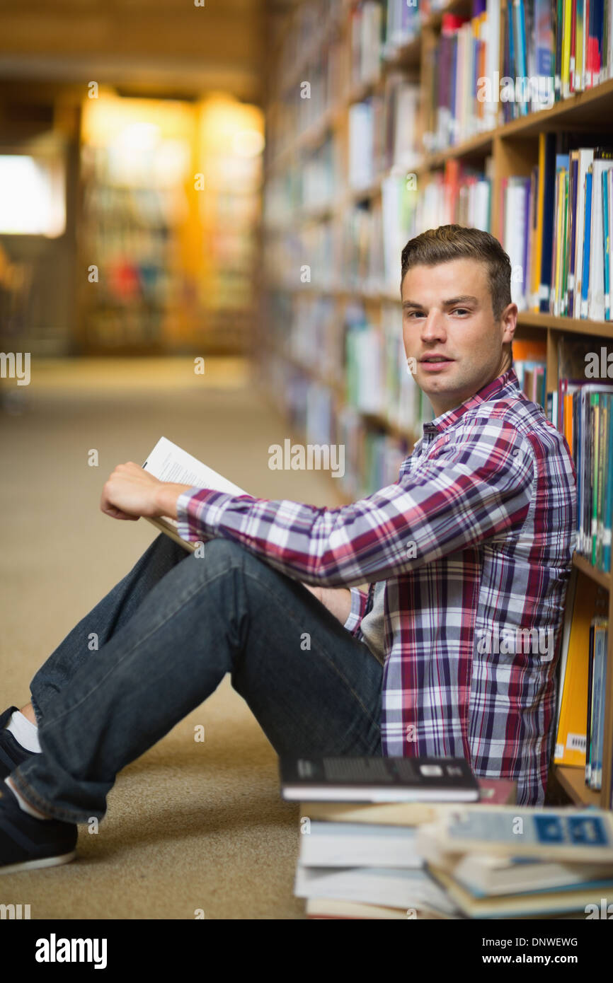Handsome student sitting on library floor reading Stock Photo - Alamy