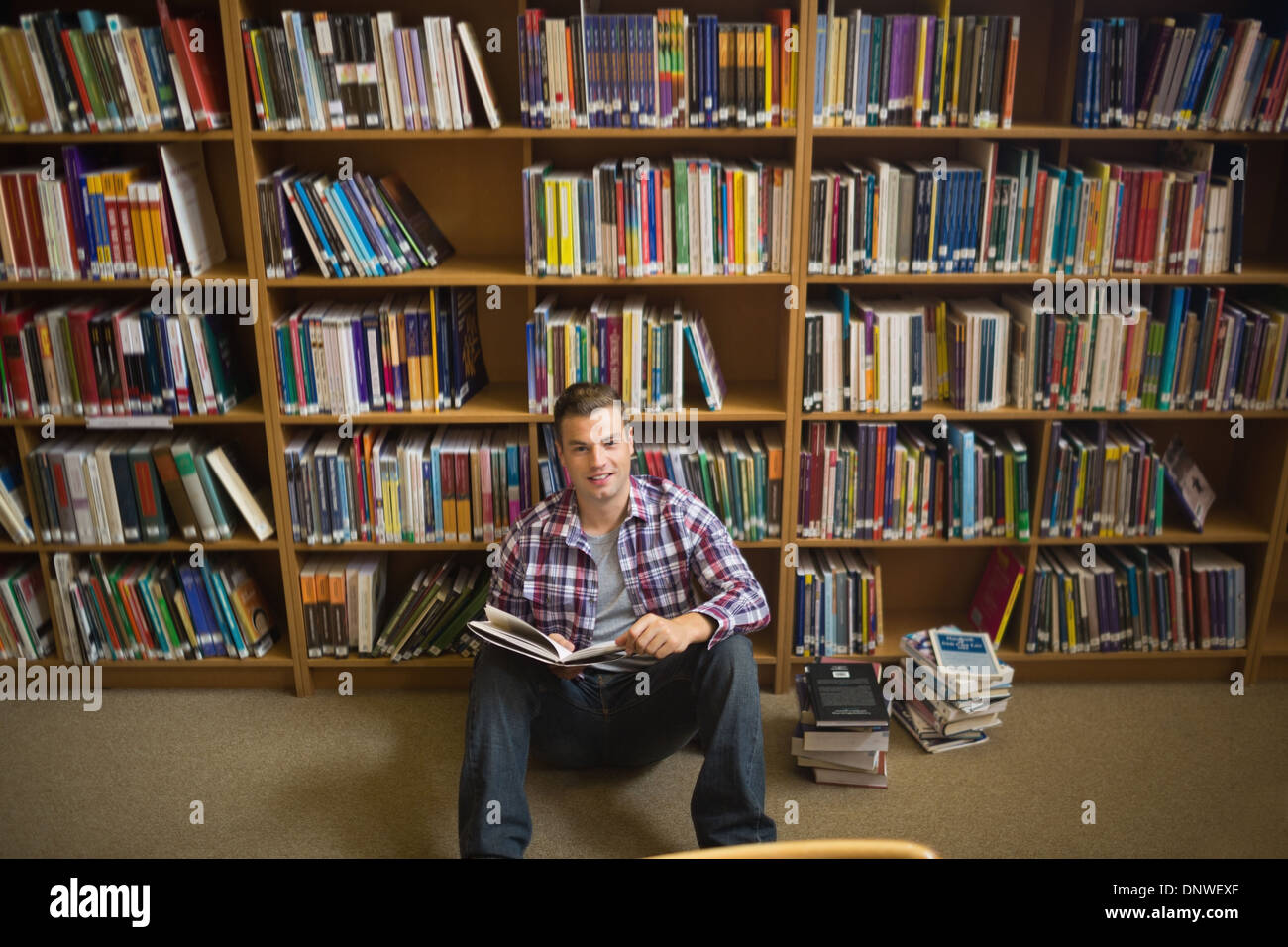 Smiling young student sitting on library floor reading Stock Photo - Alamy