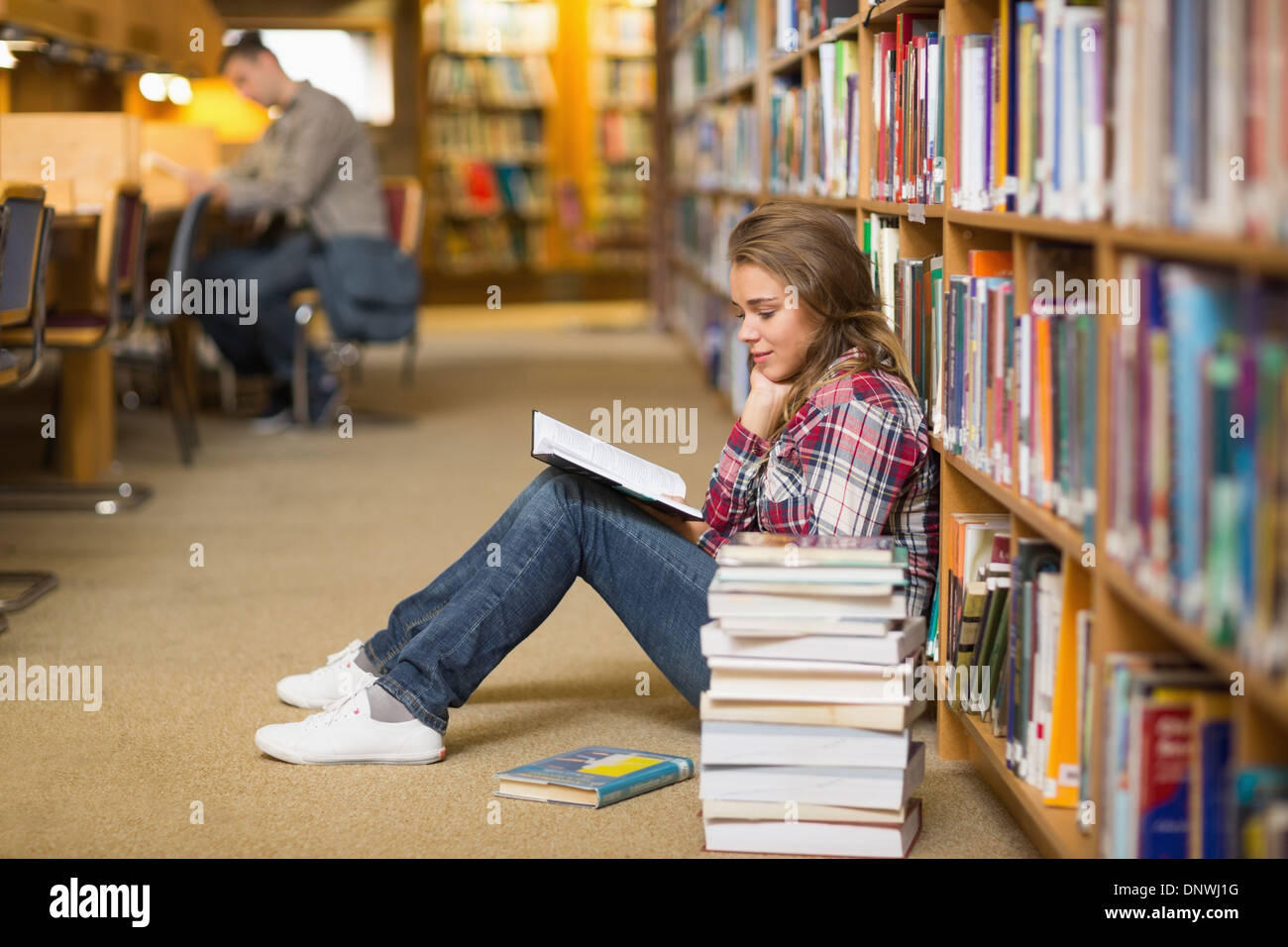Pretty student reading book on library floor Stock Photo - Alamy