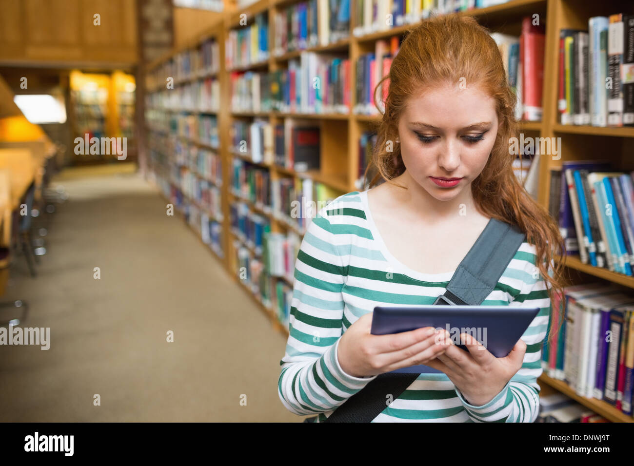 Serious student using tablet standing in library Stock Photo - Alamy