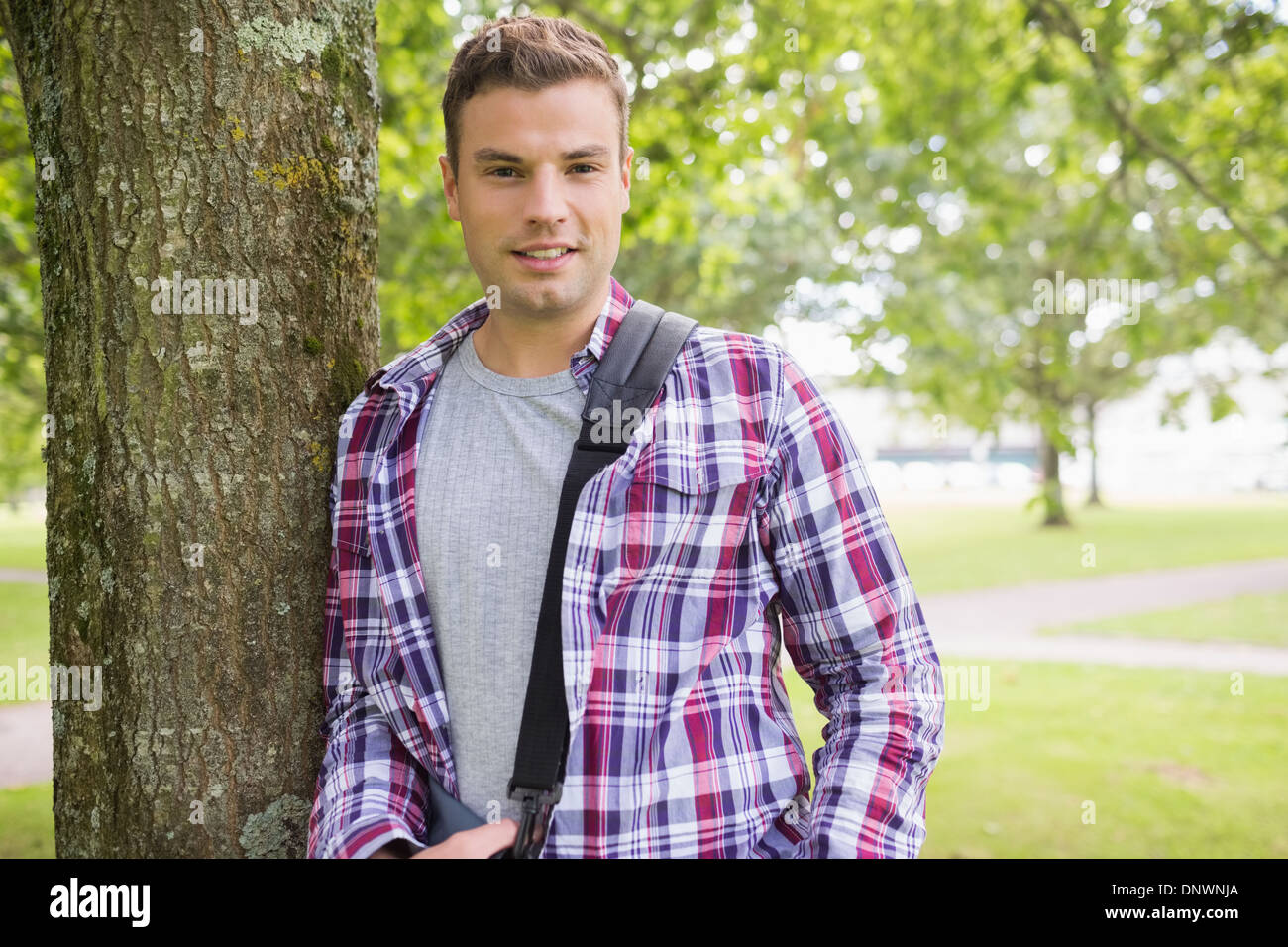 Handsome young student leaning on tree looking at camera Stock Photo ...
