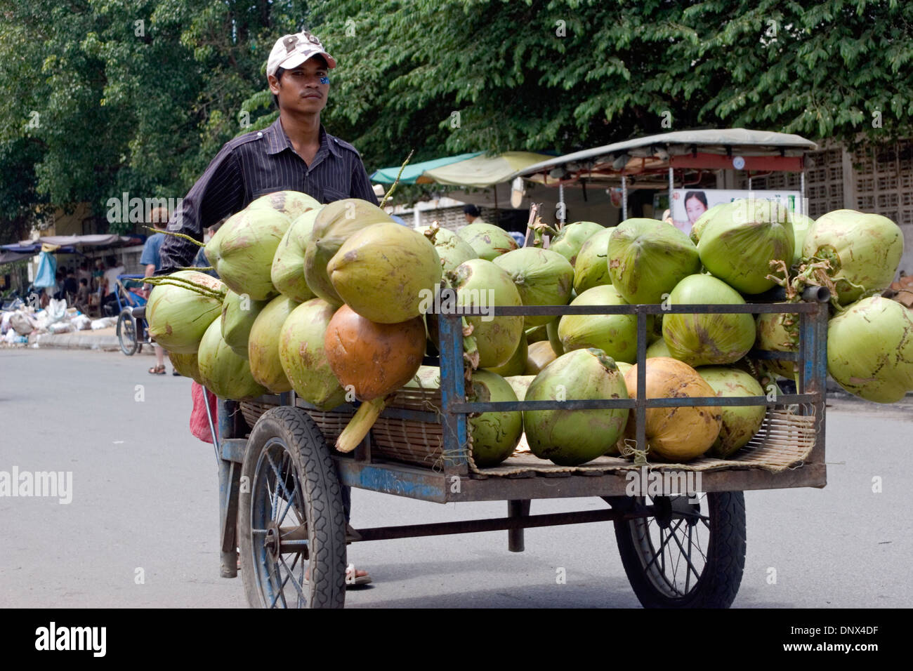 A man is selling large coconuts from a cart on a city street in Phnom ...