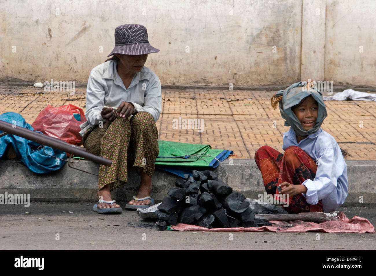 A woman and a young girl are sorting charcoal to sell on a city street ...