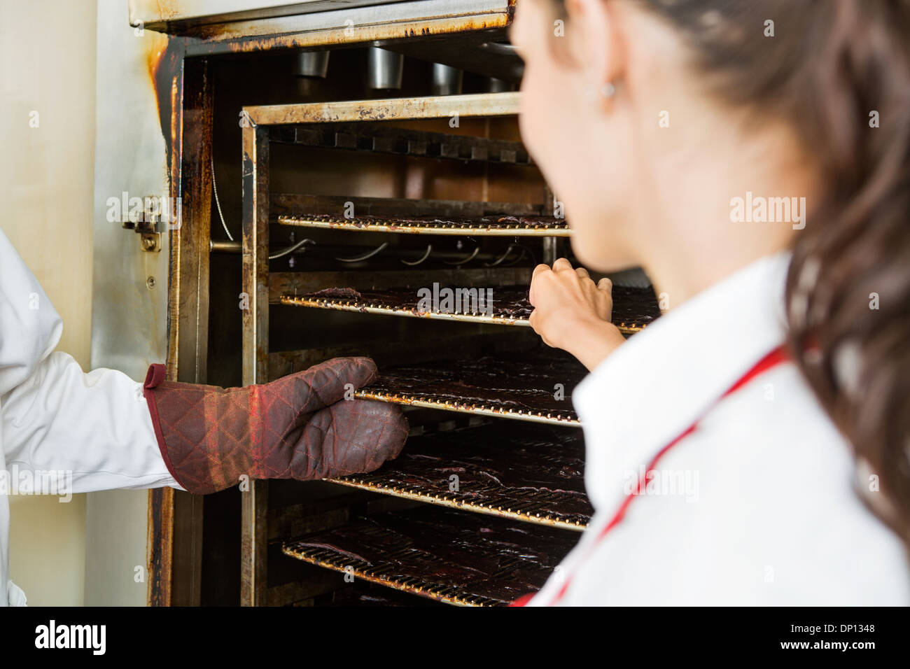 Workers Removing Dried Meat Slices From Oven At Shop Stock Photo - Alamy