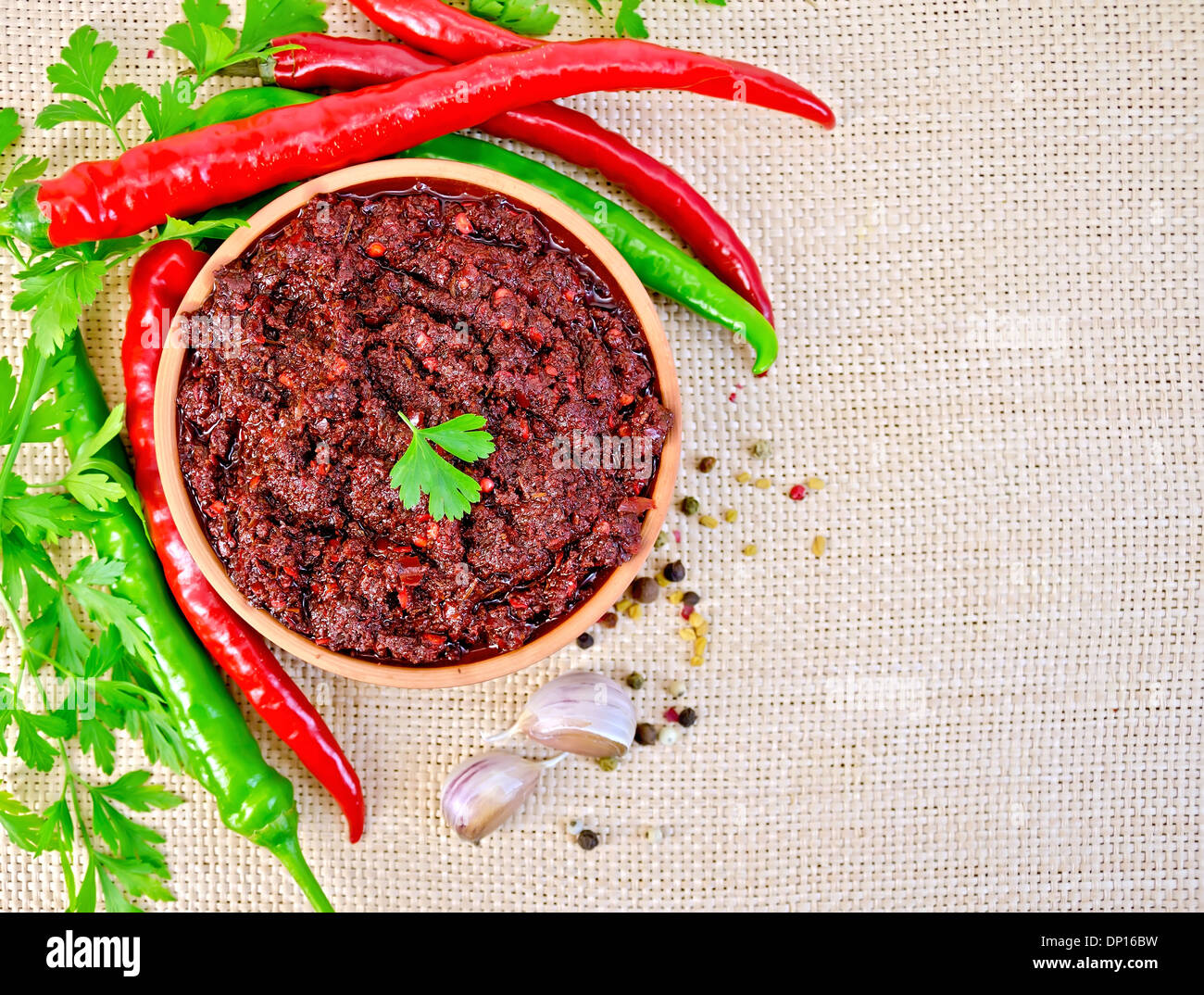 Tabasco adjika in a clay cup, different hot peppers, garlic, parsley on ...