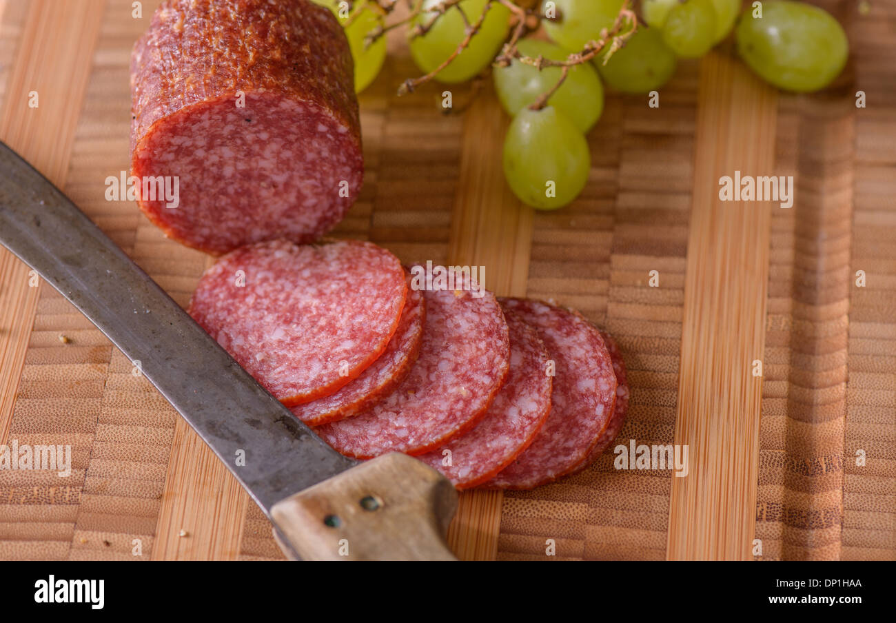 Closeup of salami with a knife and some grapes on the side Stock Photo ...