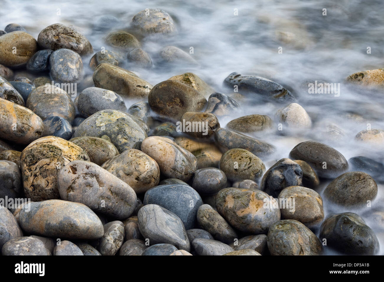 Pebbles on a beach with the sea lapping around them Stock Photo - Alamy