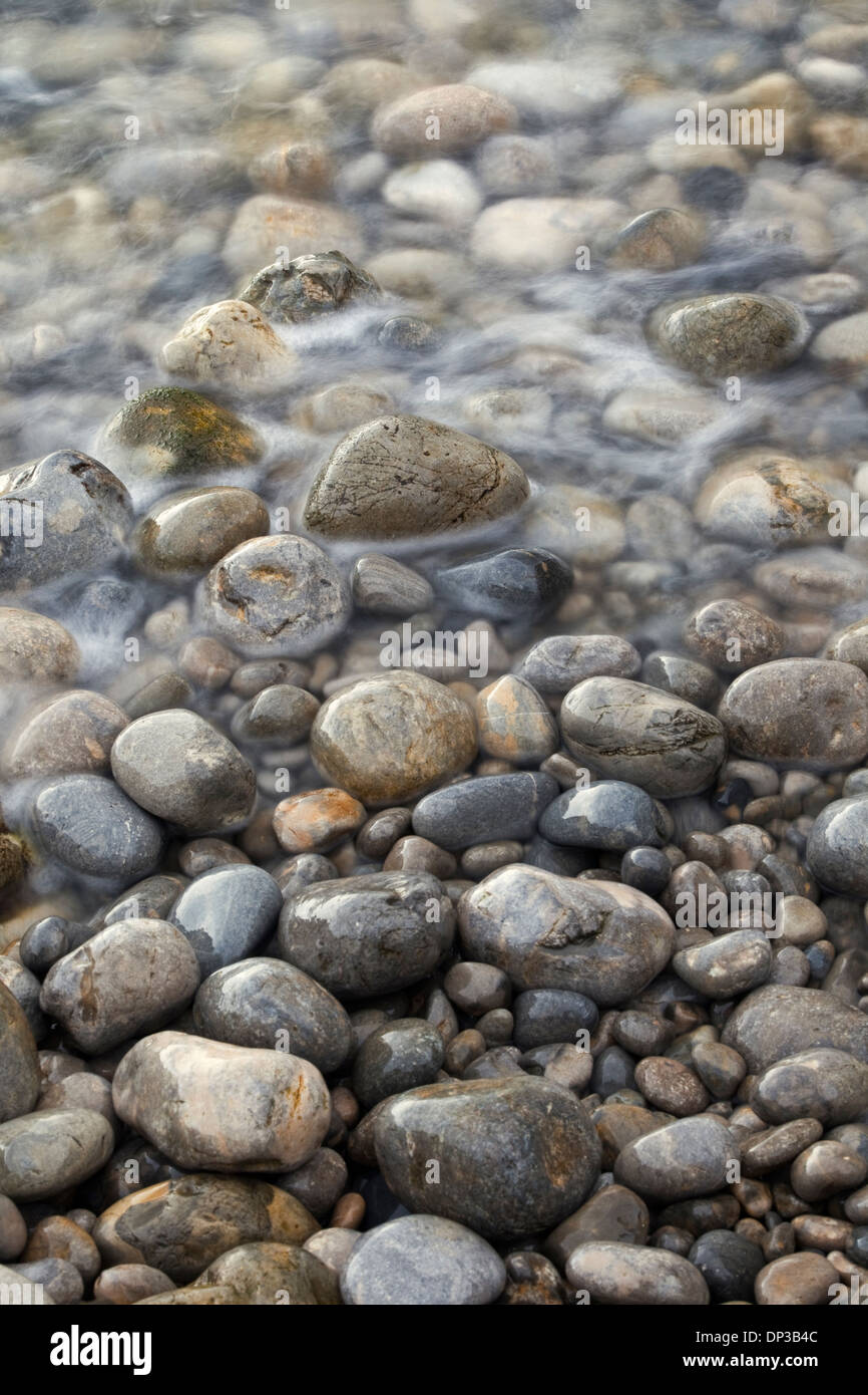 Pebbles on a beach with the sea lapping around them Stock Photo - Alamy