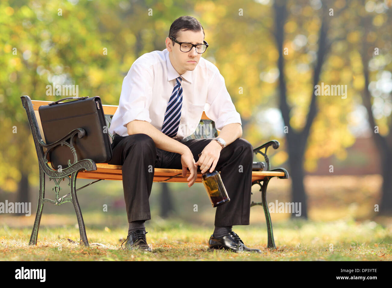 Disappointed businessman sitting on a wooden bench with bottle in his ...