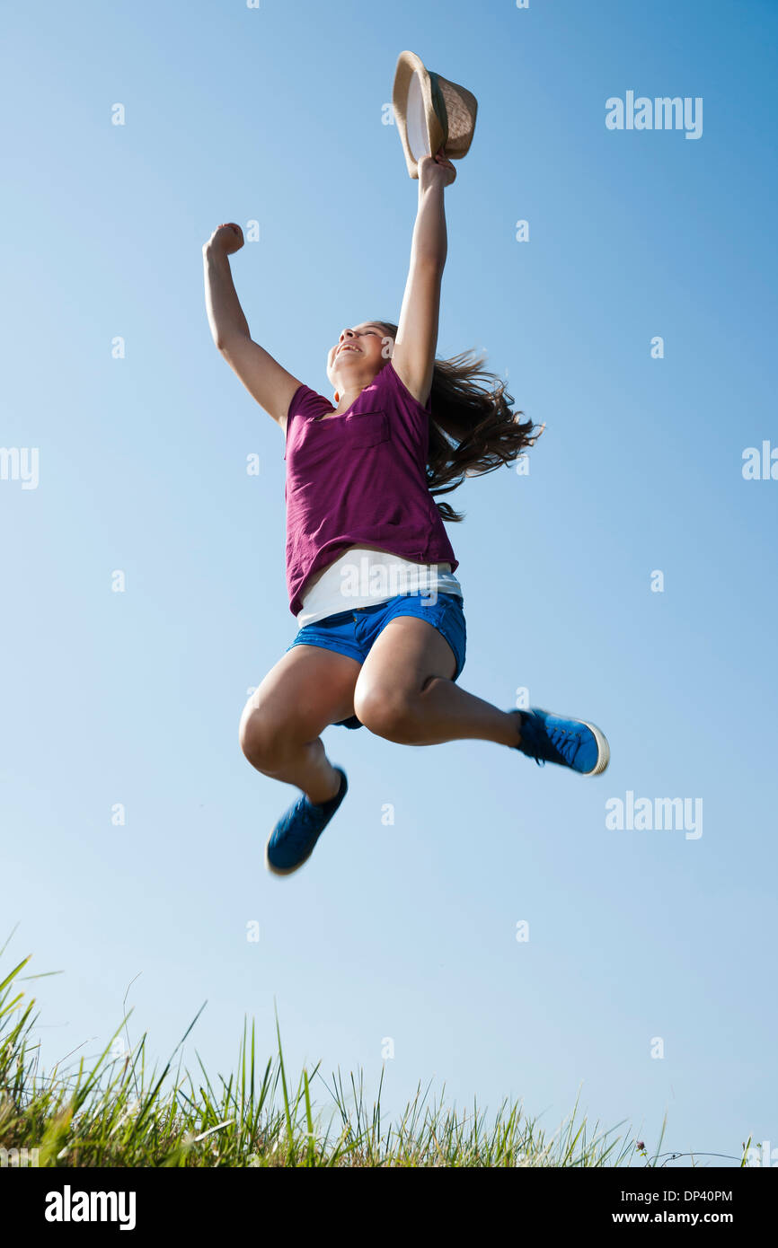 Girl holding hat, jumping in mid-air over field, Germany Stock Photo ...
