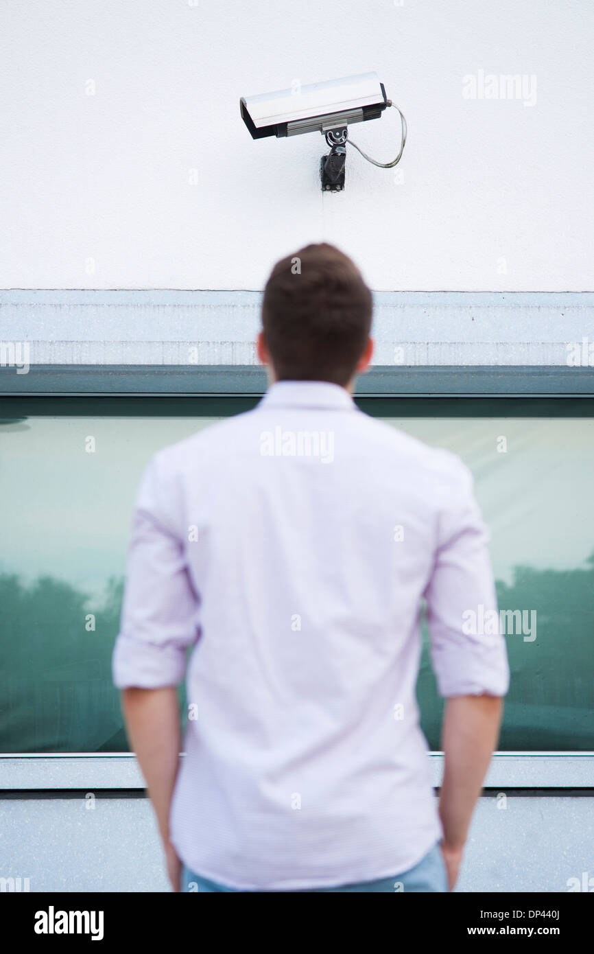 Backview of young man standing outdoors, looking at security camera ...