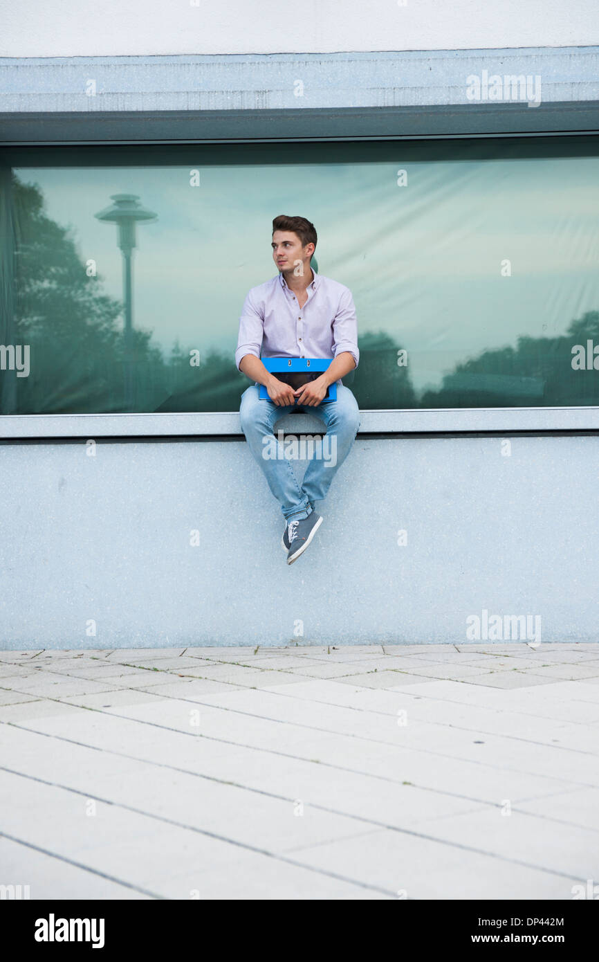 Young man sitting on ledge outdoors, Germany Stock Photo - Alamy