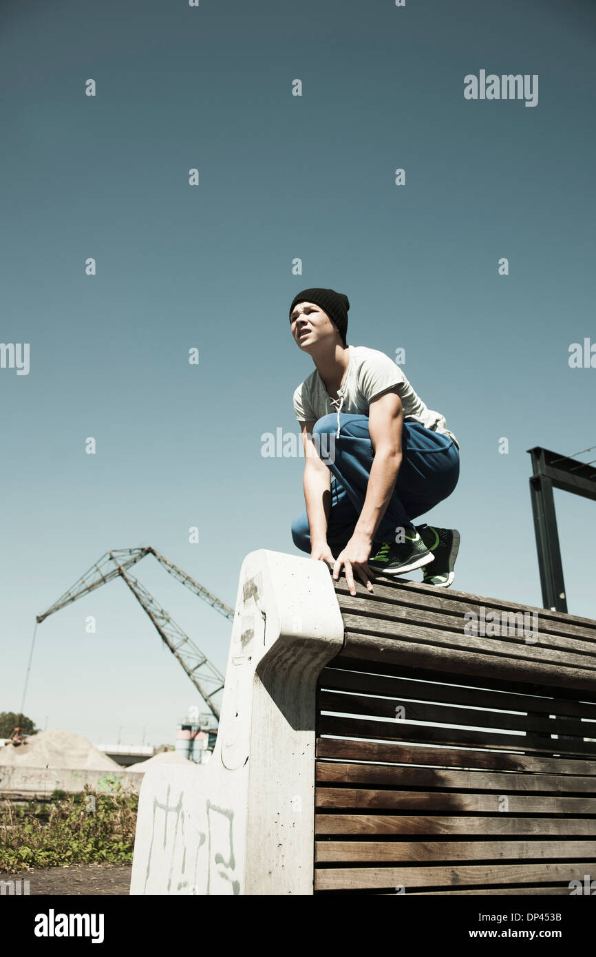 Teenager crouching down on barrier, anticipating next move, freerunning ...