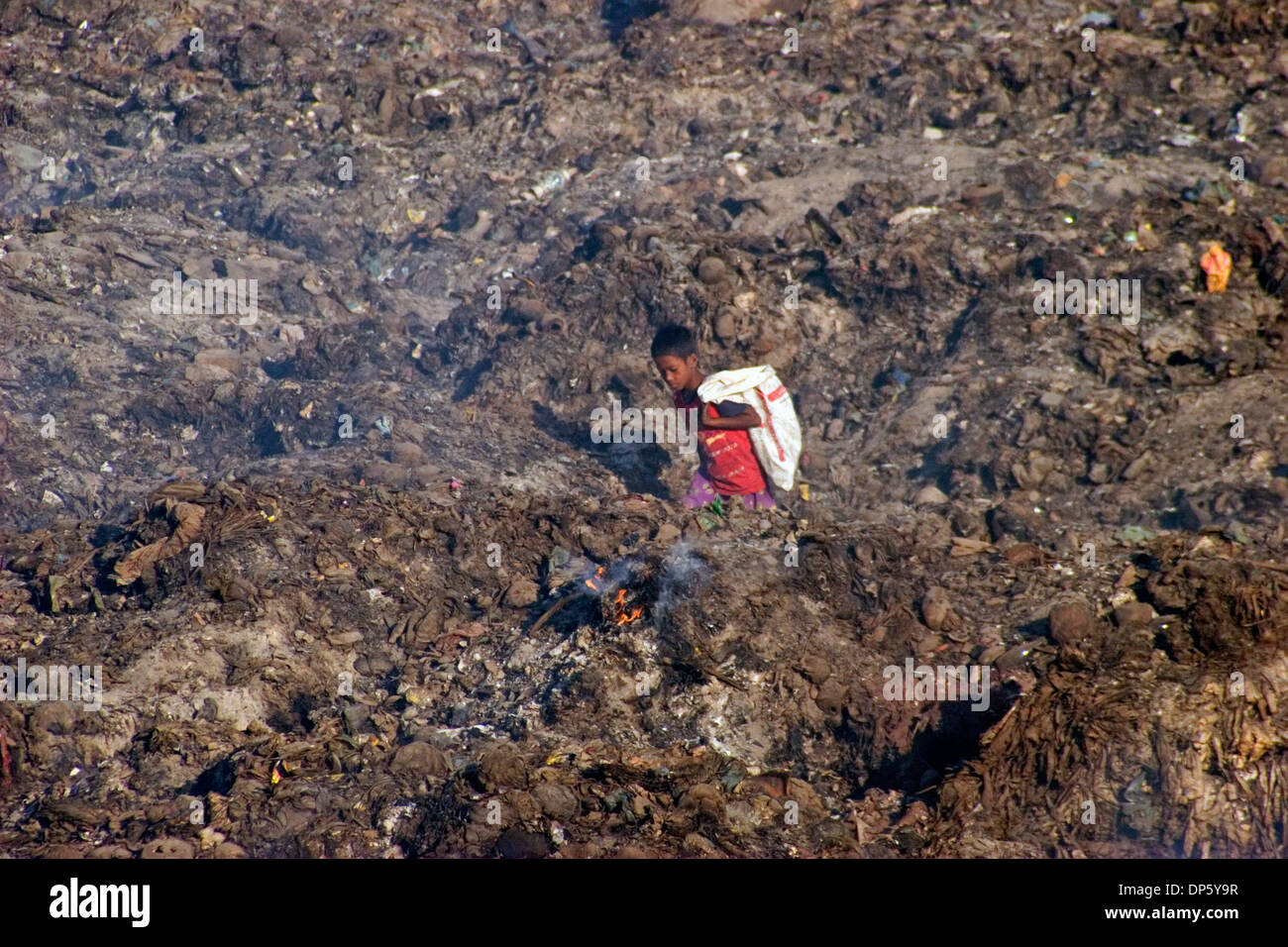 A young child laborer boy is collecting metal on burned ground at the ...