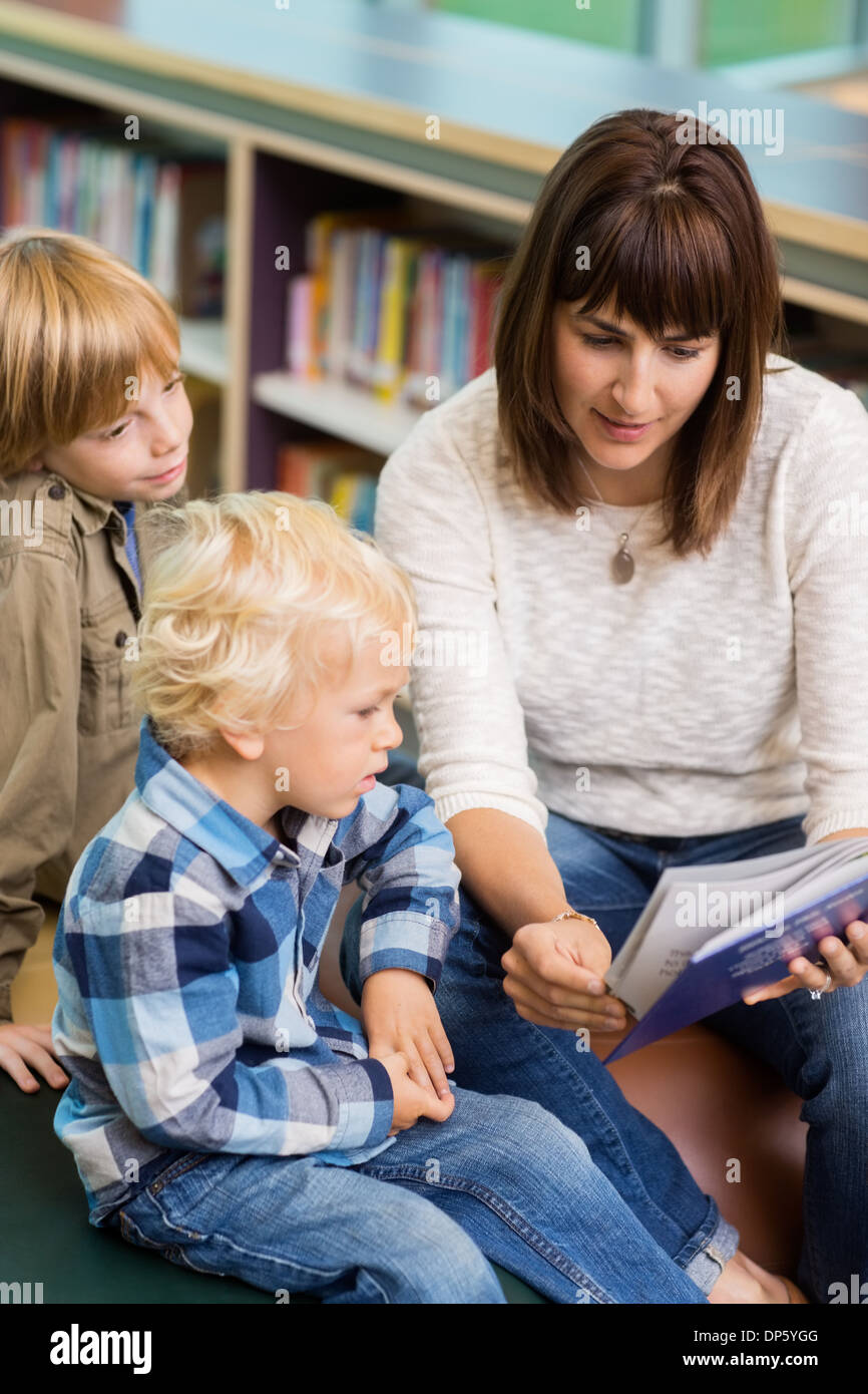 Teacher With Students Reading Book In Library Stock Photo - Alamy