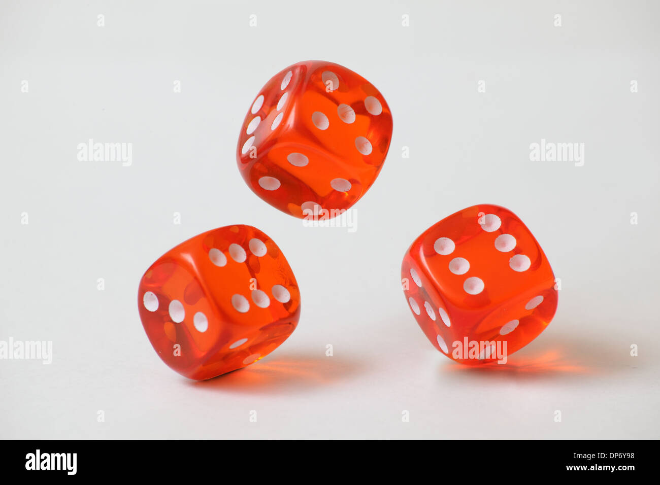 Three translucent red plastic dice tumbling on a plain white background ...