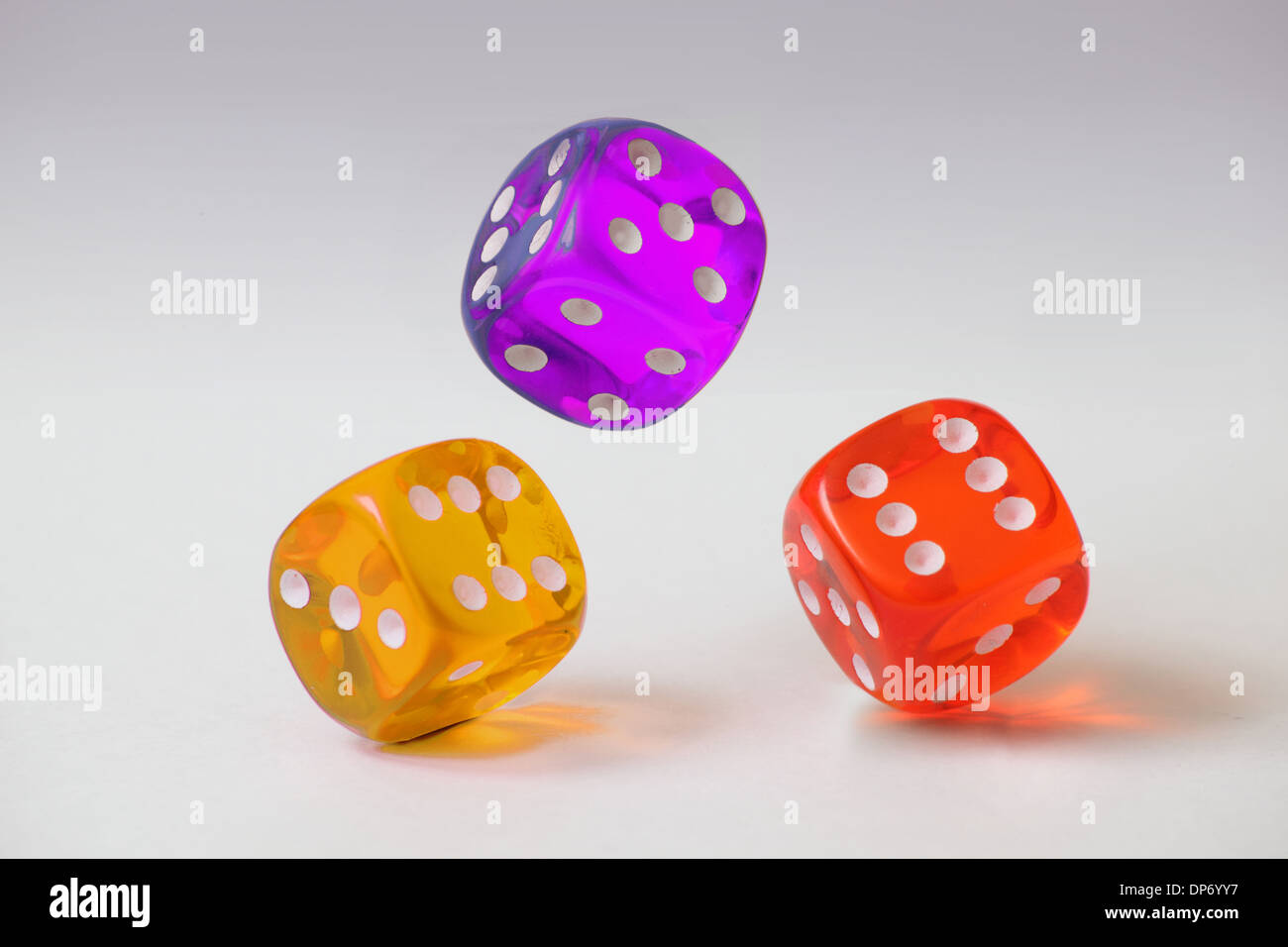 Three coloured plastic dice tumbling on a plain white graduated ...
